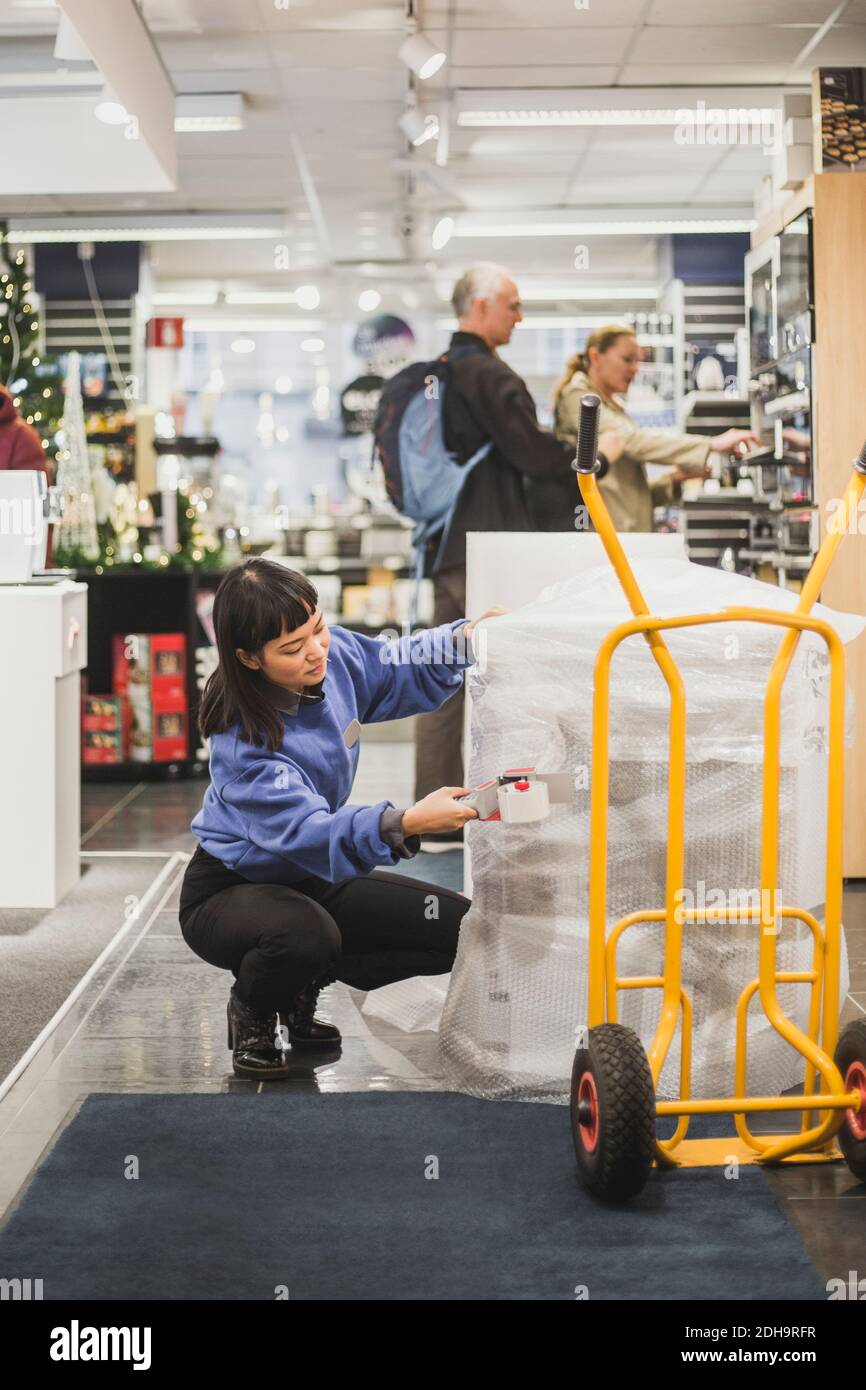 Saleswoman packing appliance while crouching in store Stock Photo - Alamy