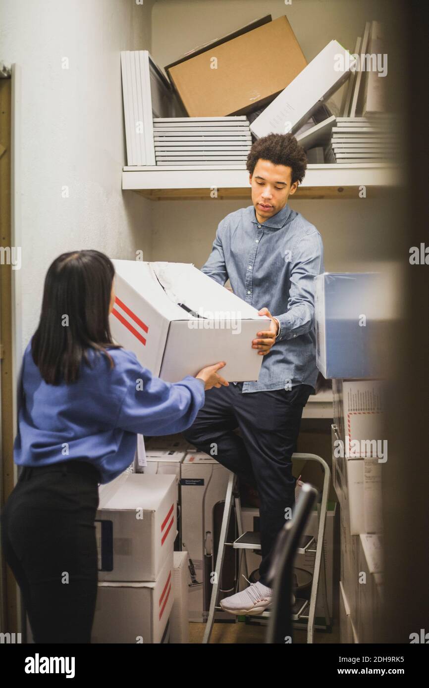 Salesman giving appliance to saleswoman while standing on ladder in ...