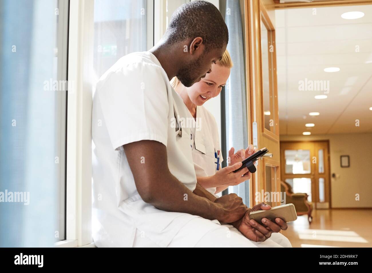 Multi-ethnic nurses using smart phone while sitting on window sill in ...