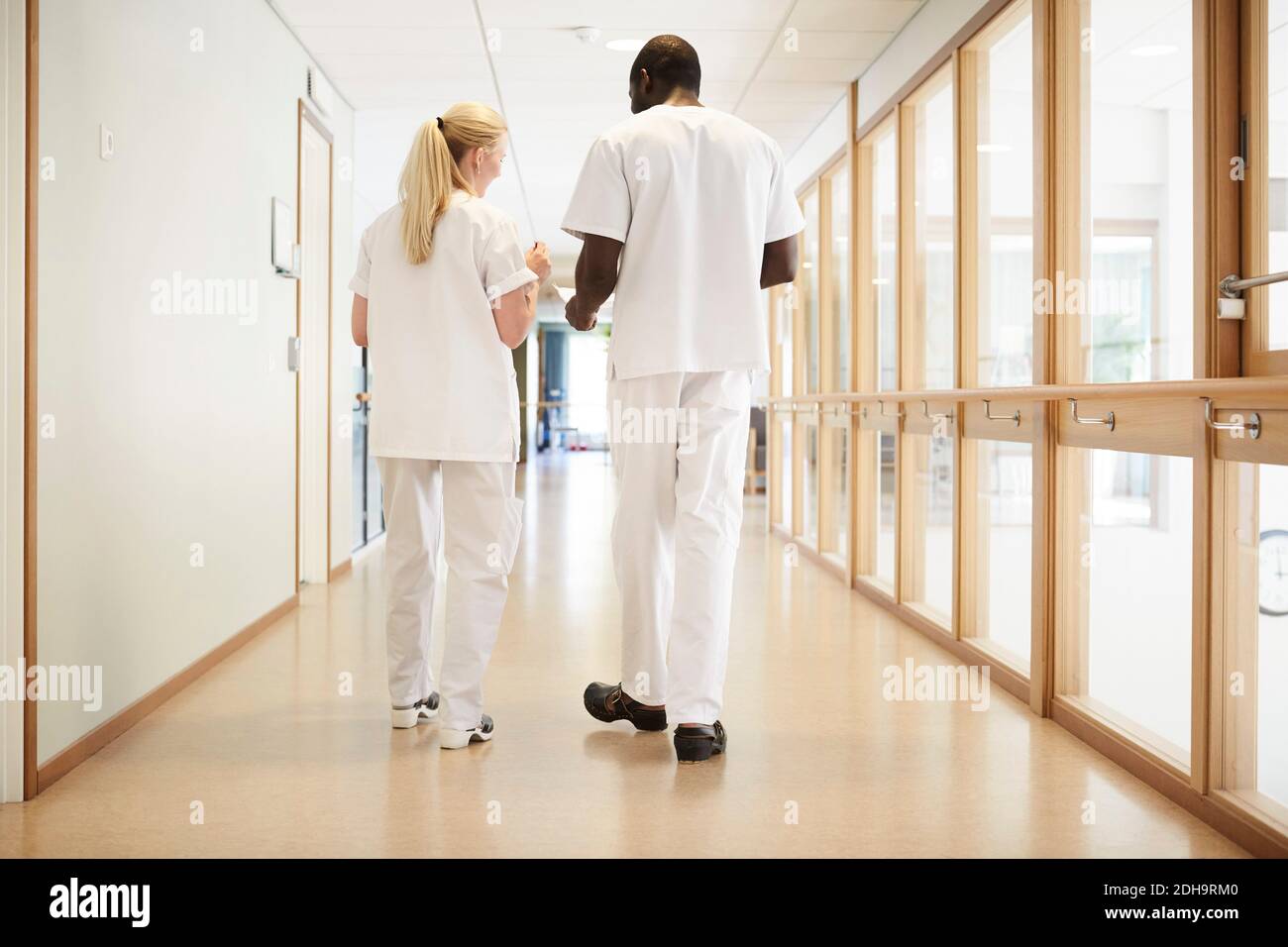 Full length rear view of male and female nurse walking in hospital ...
