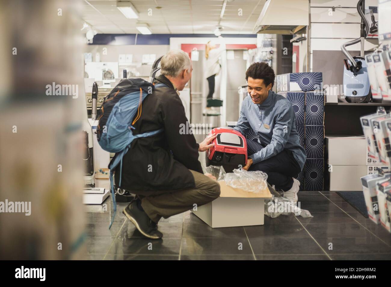 Smiling young salesman showing appliance to male customer in store ...