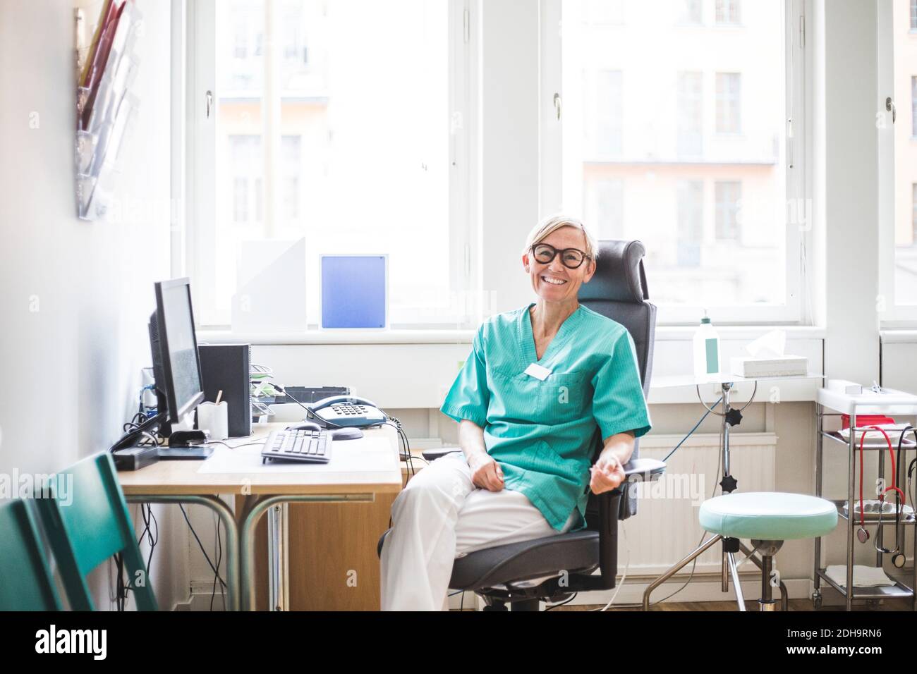 Portrait of smiling mature female doctor sitting in clinic Stock Photo ...