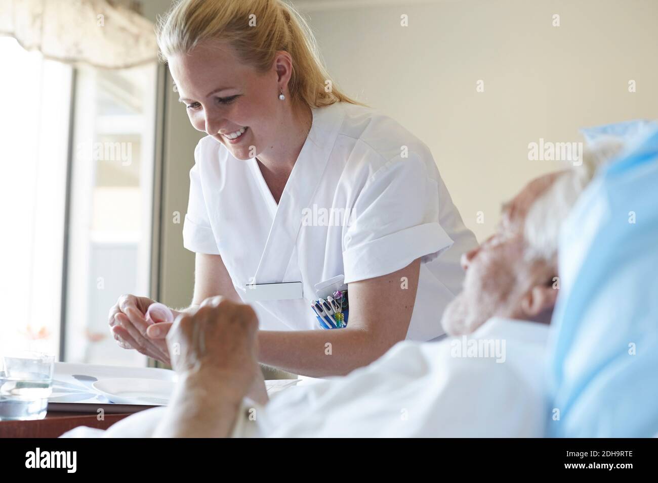 Happy Female Nurse Giving Cough Syrup To Senior Man In Hospital Ward