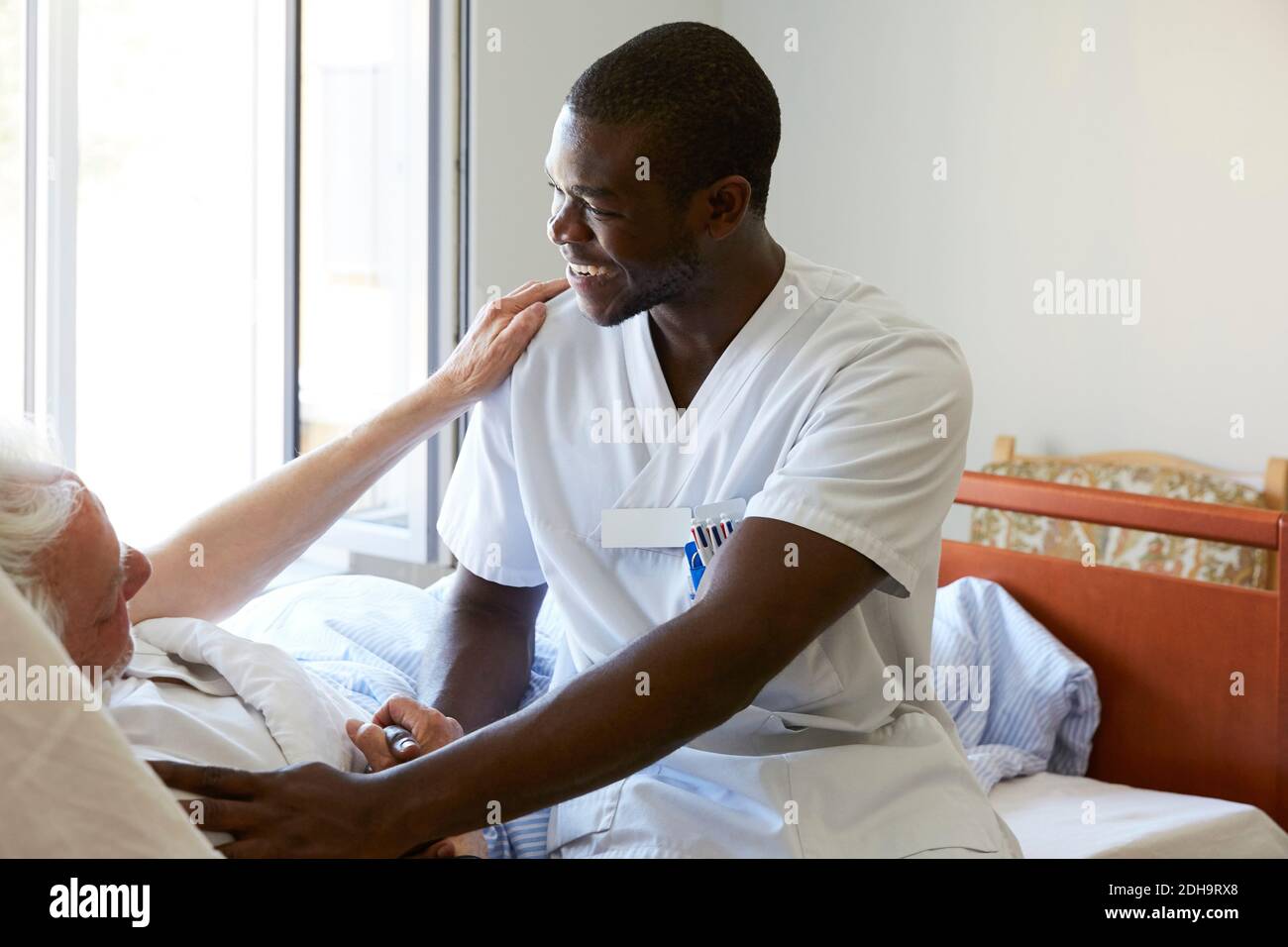 Smiling male nurse consoling senior man in hospital ward Stock Photo ...