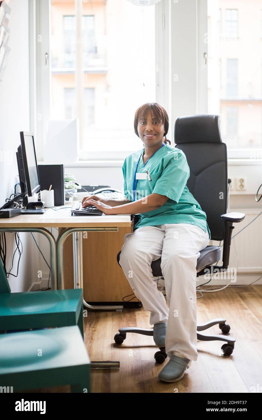 Portrait of mature female doctor working over computer while sitting in ...