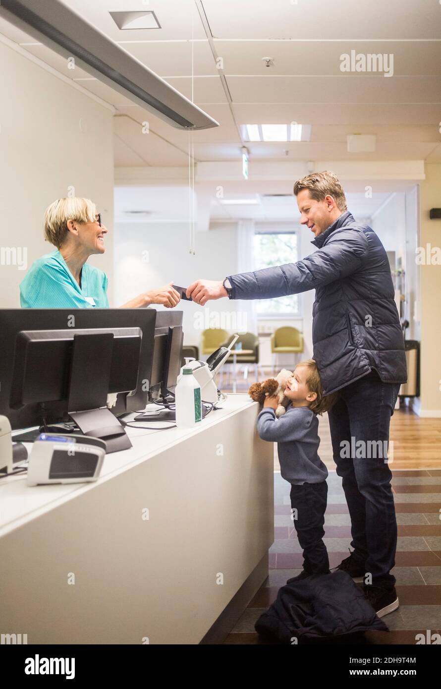 Side view of mature man giving id card to doctor while son standing by ...