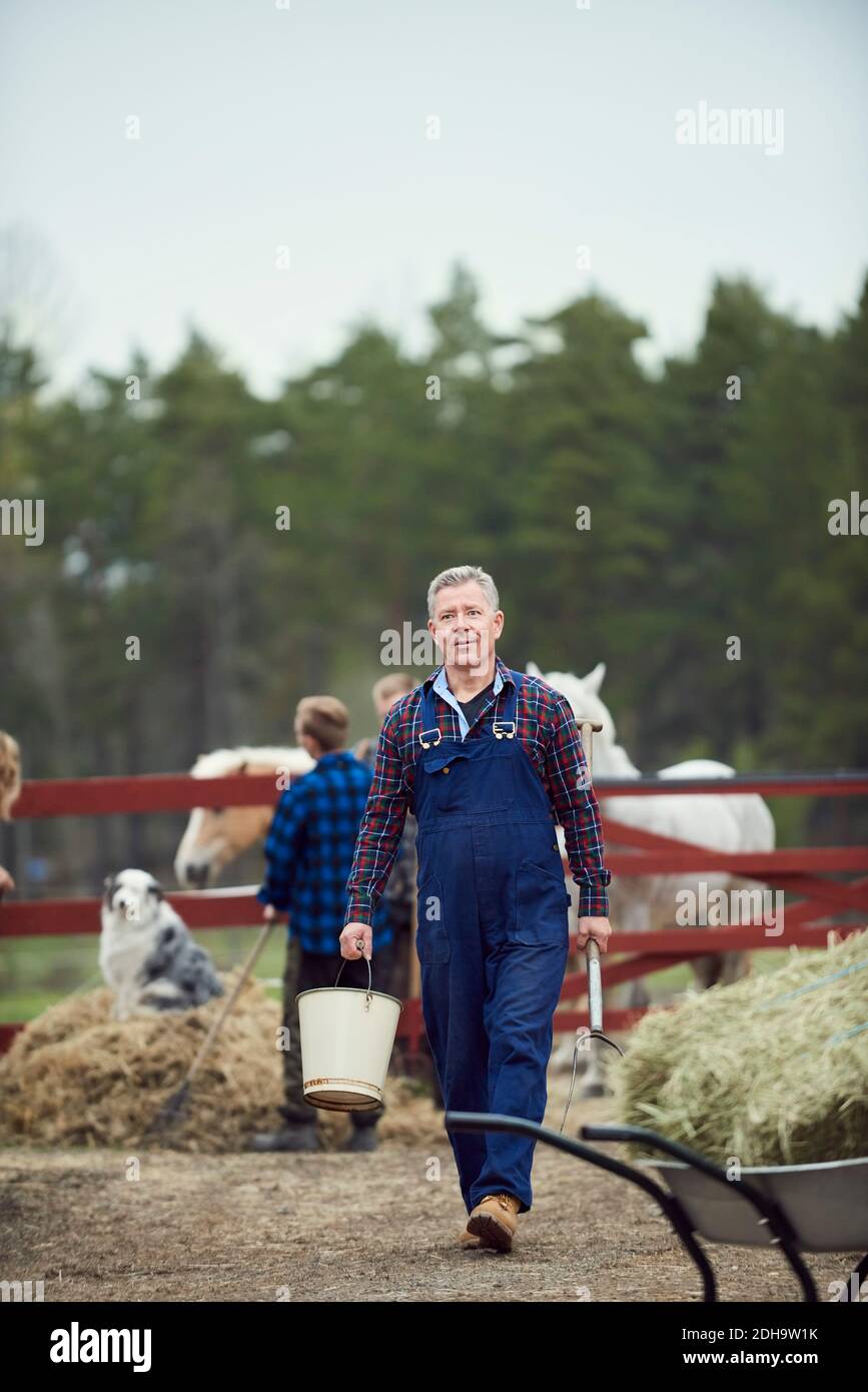 Farmer carrying bucket and pitchfork while walking in farm Stock Photo ...