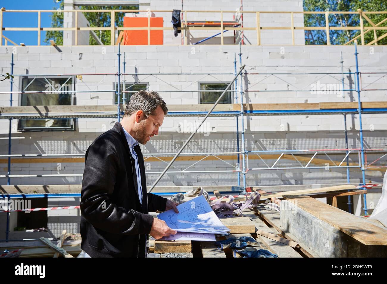 Side view of architect reading blueprint by incomplete building at ...