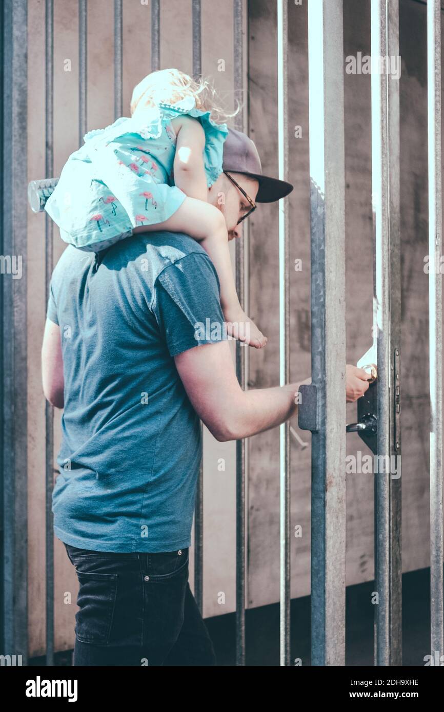 Rear view of man opening gate while carrying daughter on shoulders ...