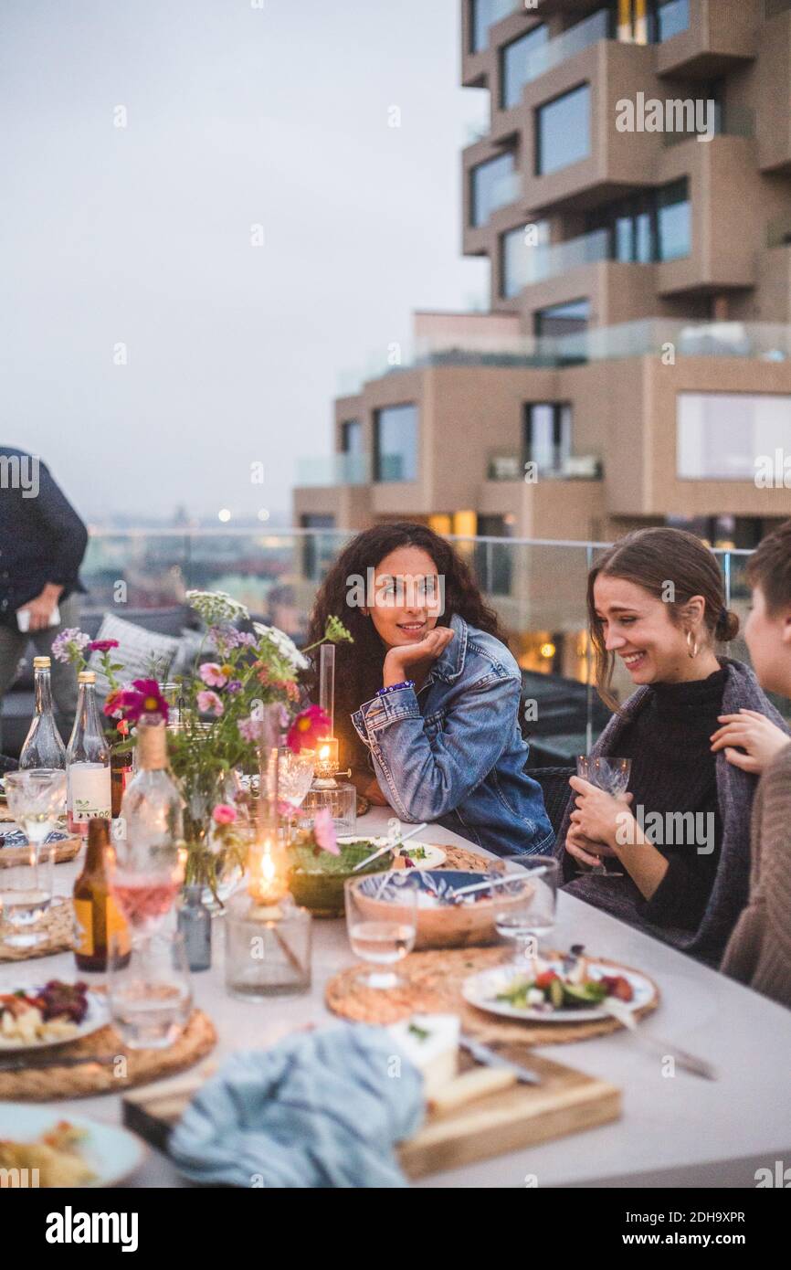 Happy female sitting with friends while talking on building terrace ...