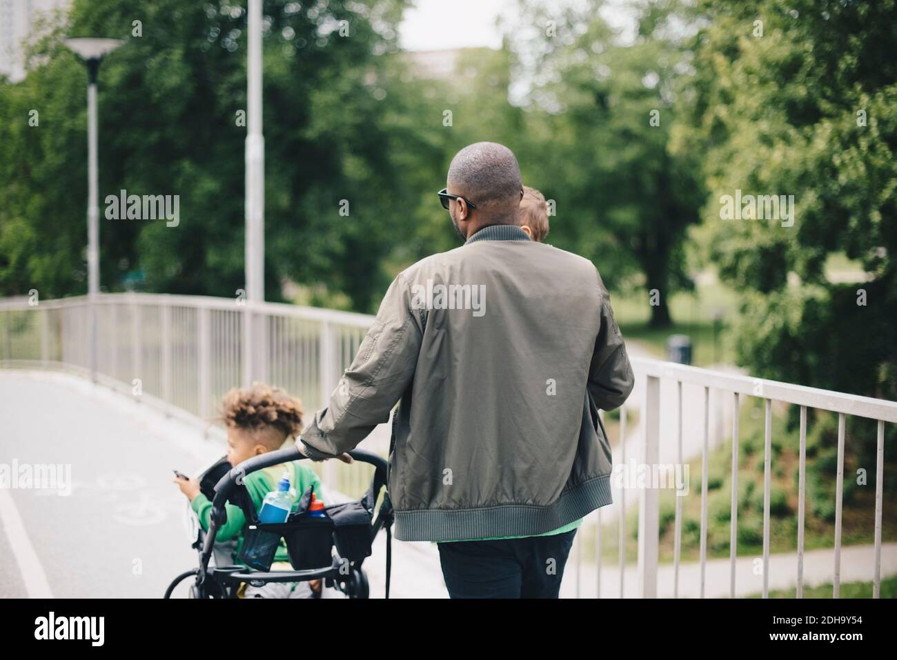 Rear view of father pushing baby stroller while walking with sons on ...
