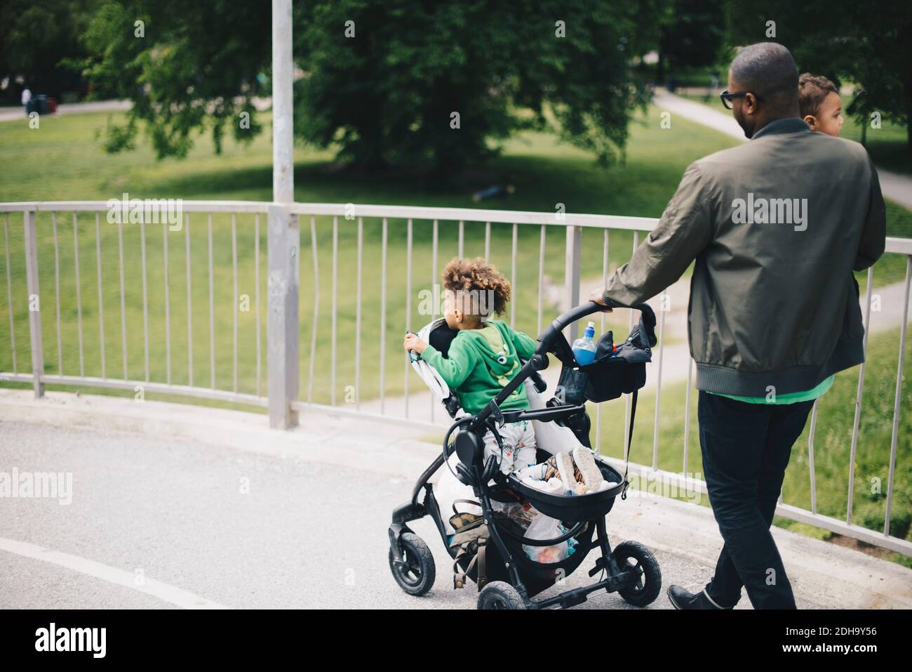 Father walking with children while pushing baby stroller on bridge ...