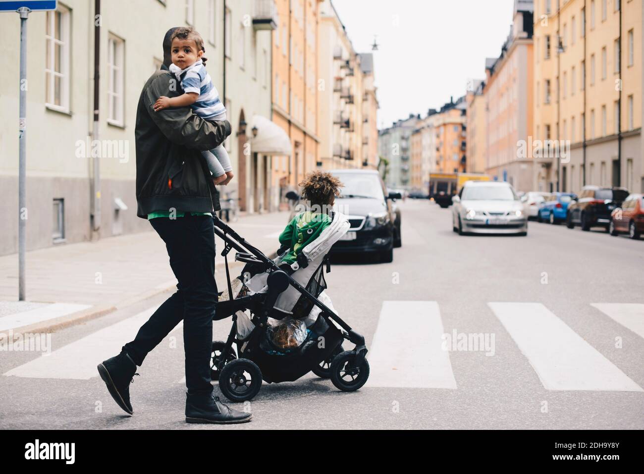 Father crossing road with children while pushing baby stroller in city ...