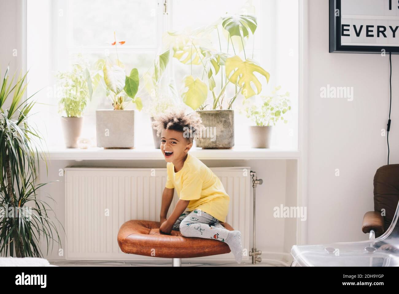 Happy boy sitting on chair by window at home Stock Photo - Alamy