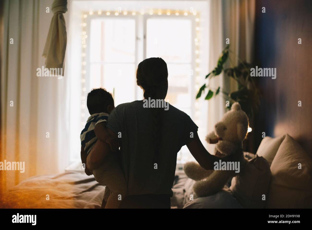 Woman keeping teddy bear on bed while carrying son at bedroom Stock ...