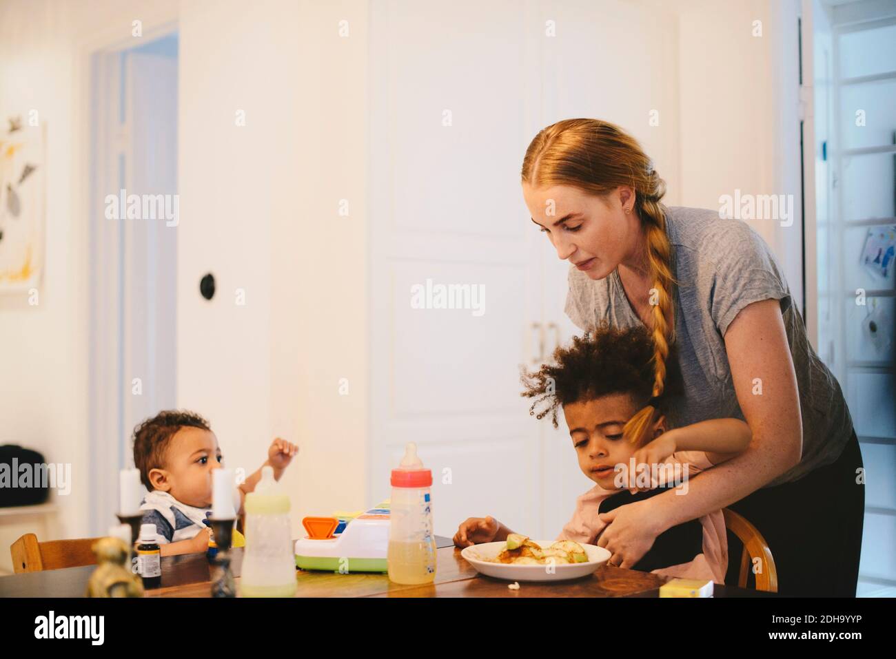 Toddler looking at mother giving food to brother at home Stock Photo ...