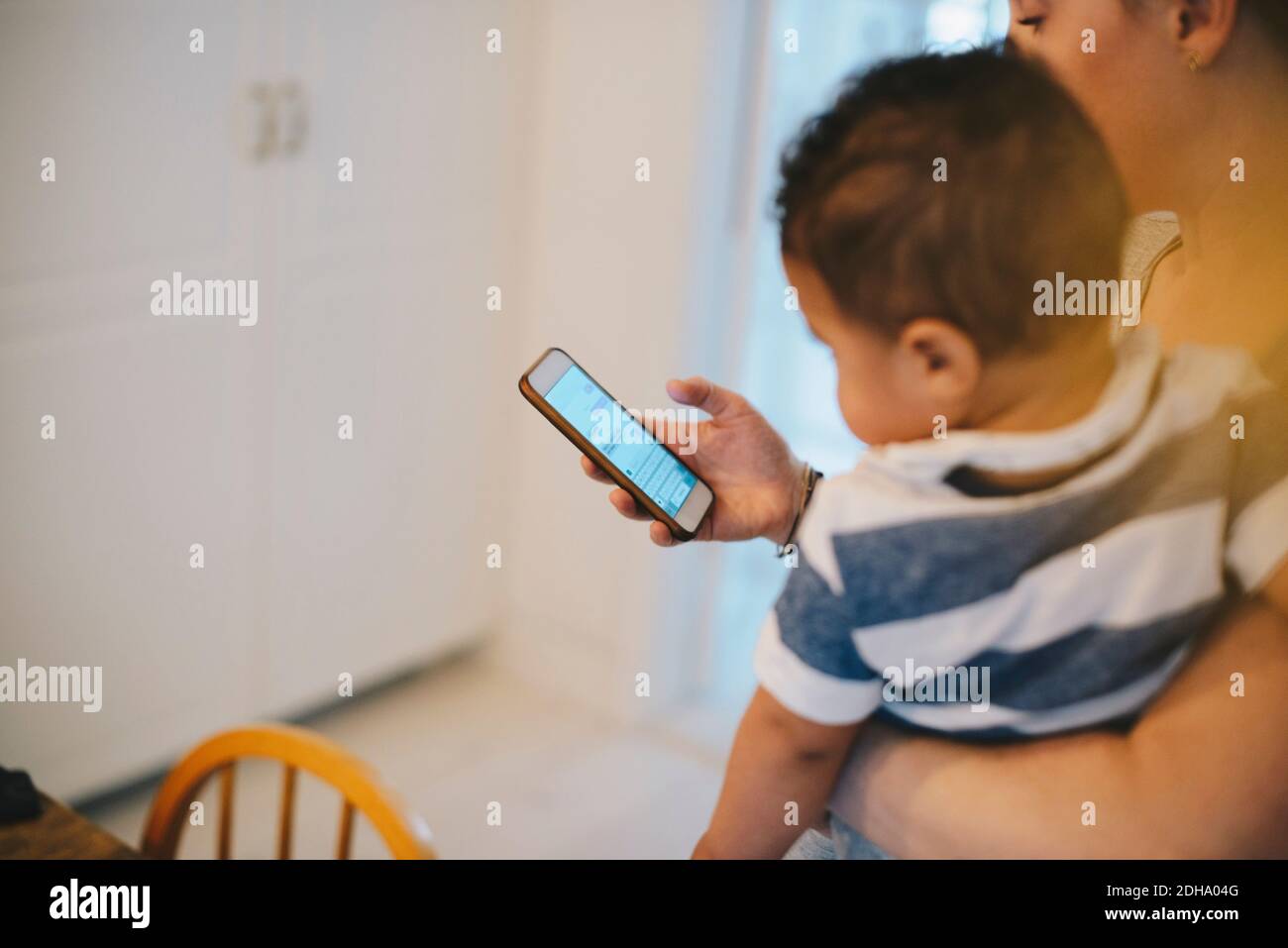 Mother using mobile phone while carrying son at home Stock Photo - Alamy