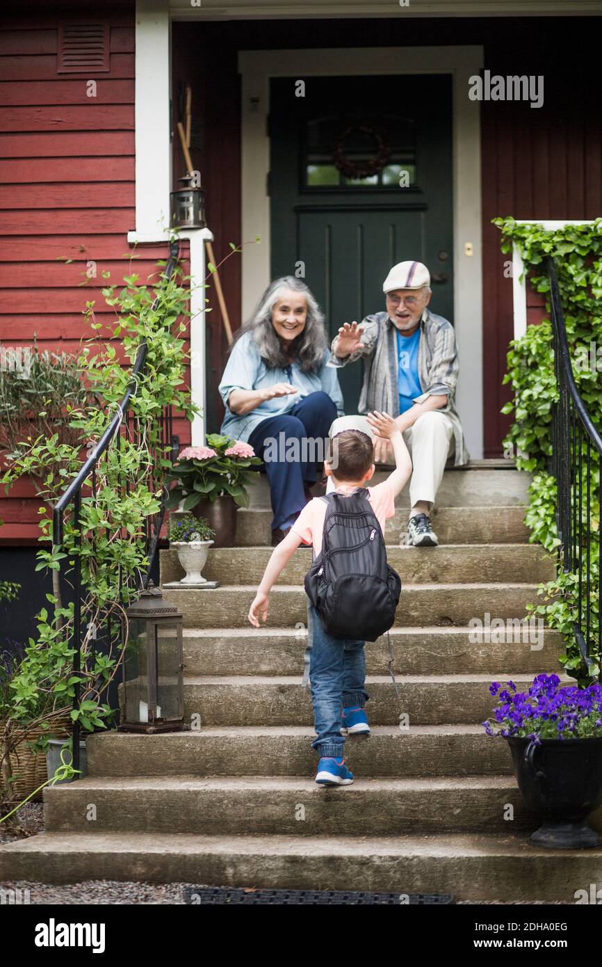 Rear view of boy waving at grandparents sitting on front stoop Stock ...
