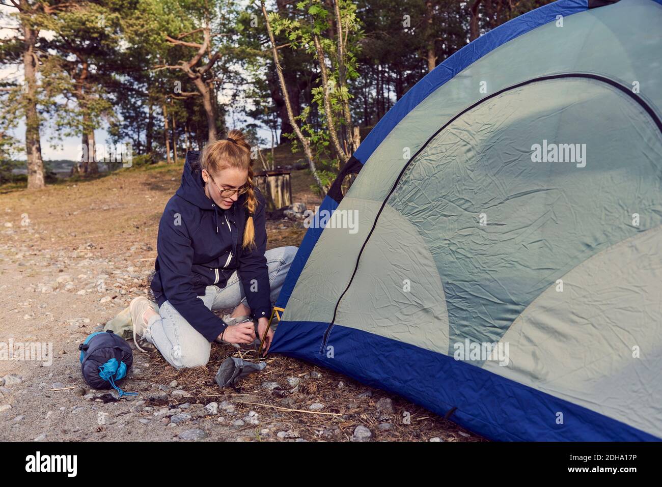 Young woman kneeling while setting up tent at campsite Stock Photo - Alamy