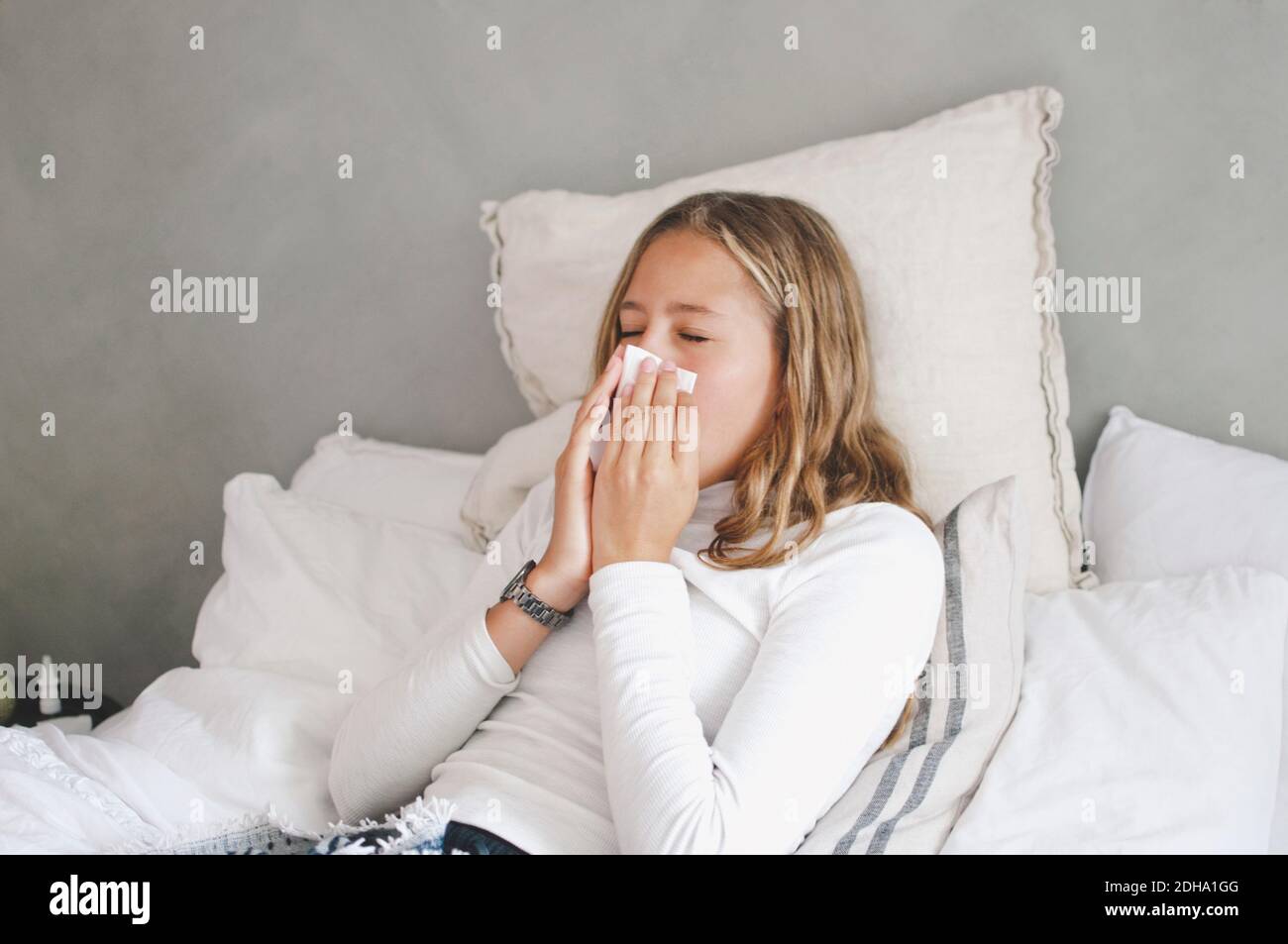 Girl blowing nose while lying on bed at home Stock Photo - Alamy