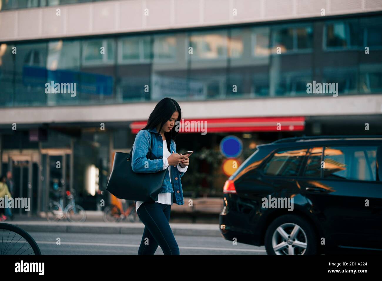 Teenage girl walking while using smart phone against building in city ...
