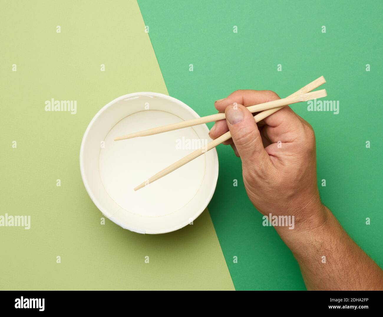 Pair of wooden chopsticks in a male hand and empty paper plate on a ...