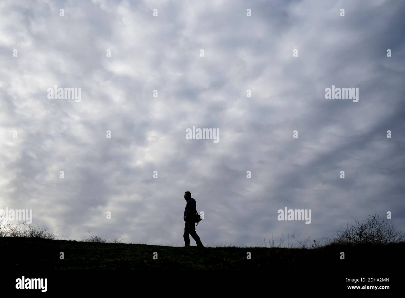 Side view silhouette of a man walking against a dark cloudy background ...