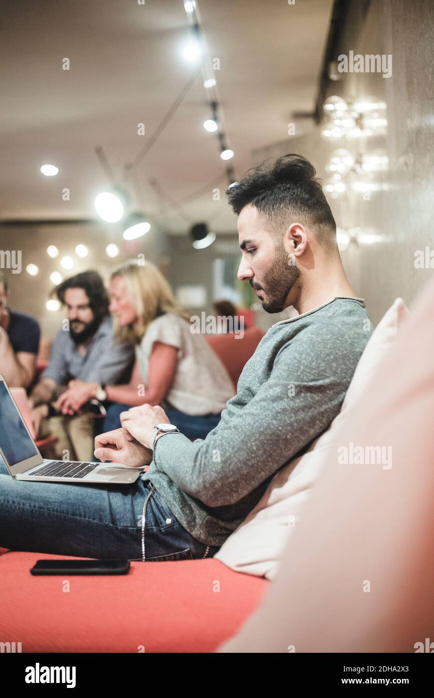 Side view of businessman working over laptop while sitting on sofa at ...