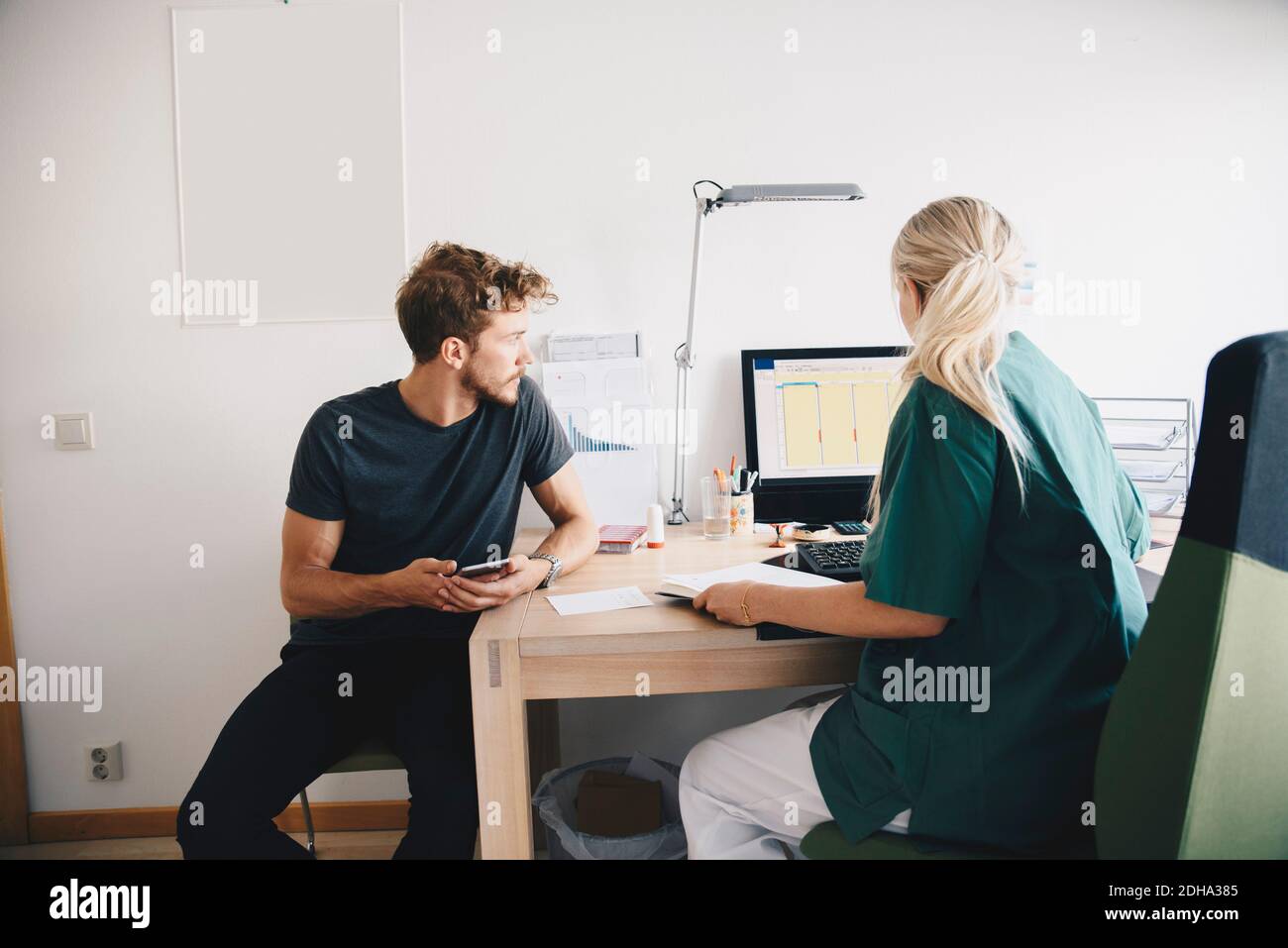 Male patient looking while female nurse using computer at office in ...