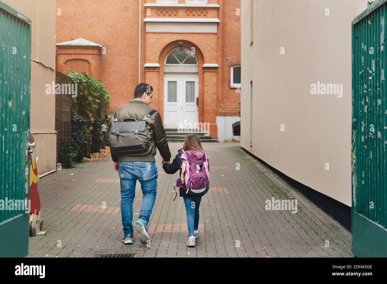 Rear view of father and daughter with backpack walking towards school ...