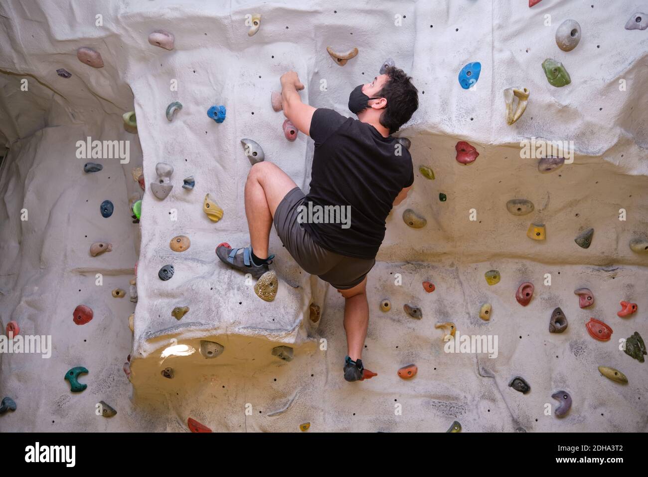 Active sporty man wearing protective face mask practicing rock climbing ...