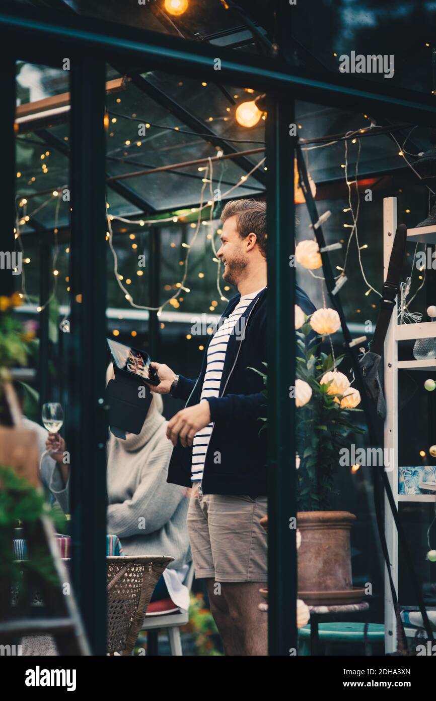 Smiling young man standing with digital tablet by woman at dining table ...