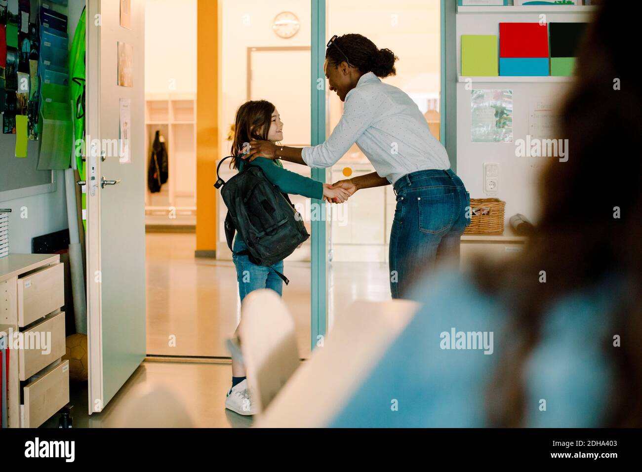Smiling female teacher shaking hands with student in classroom Stock ...