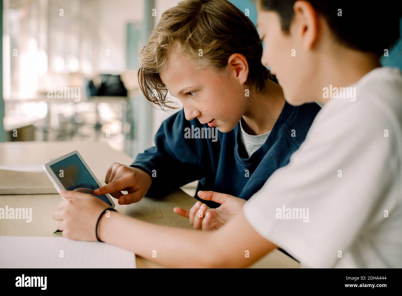 Male student pointing at digital tablet while sitting with friend in ...