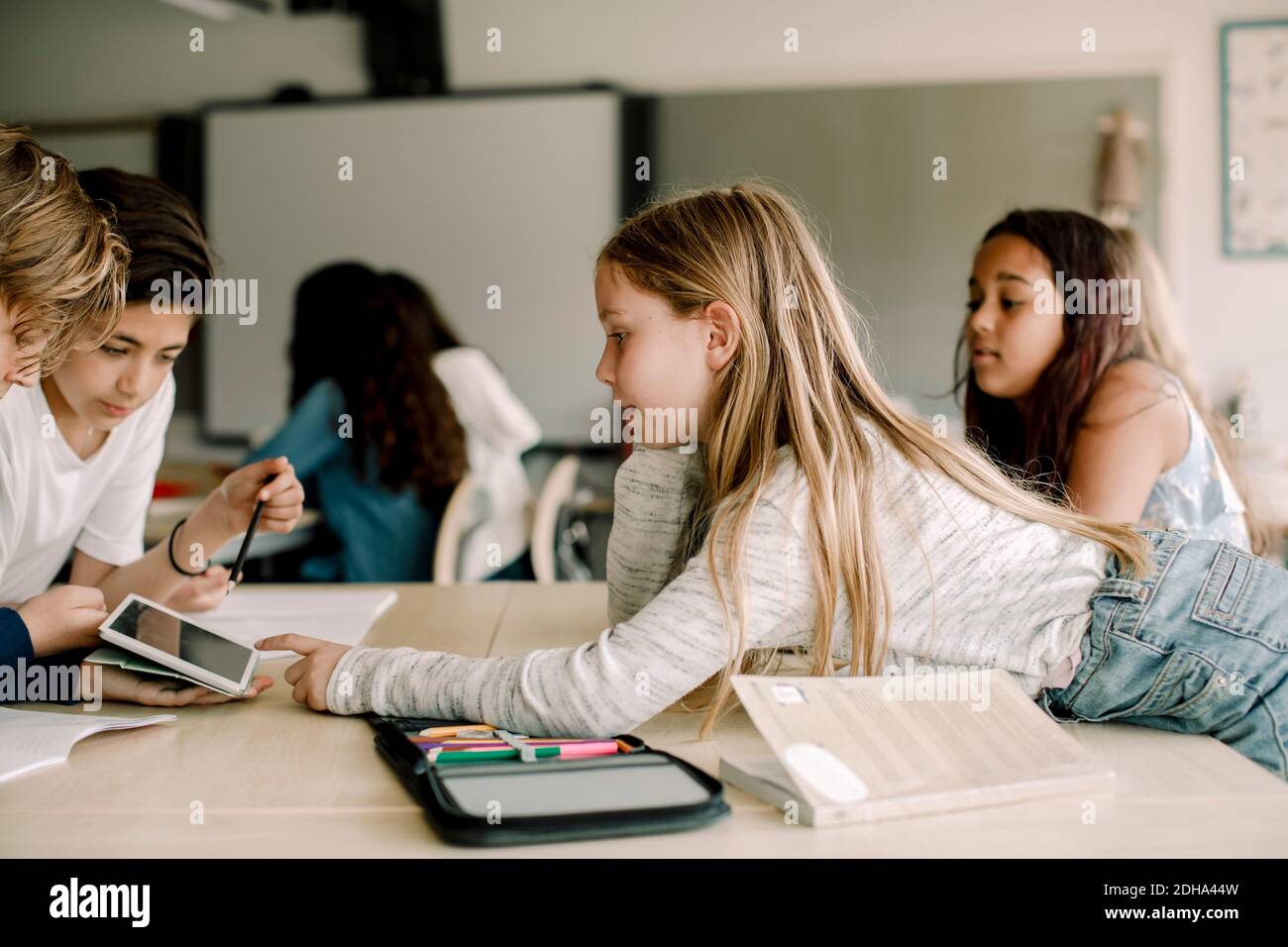 Female student pointing at digital tablet while leaning over table in ...