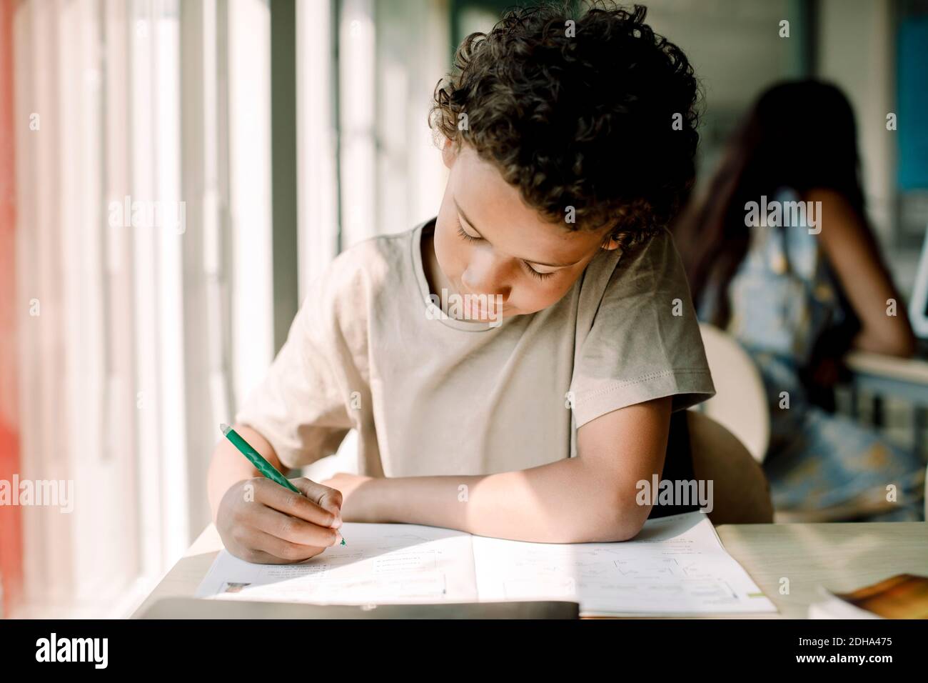 Male student writing while sitting in classroom Stock Photo - Alamy