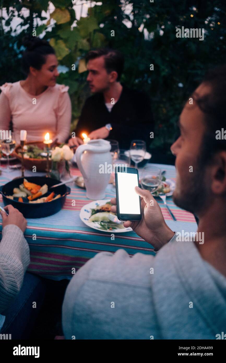 Young man holding mobile phone while friends communicating at dining ...
