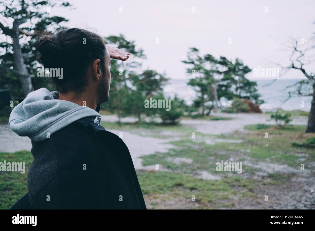 Side view of young man shielding eyes on field at beach Stock Photo - Alamy
