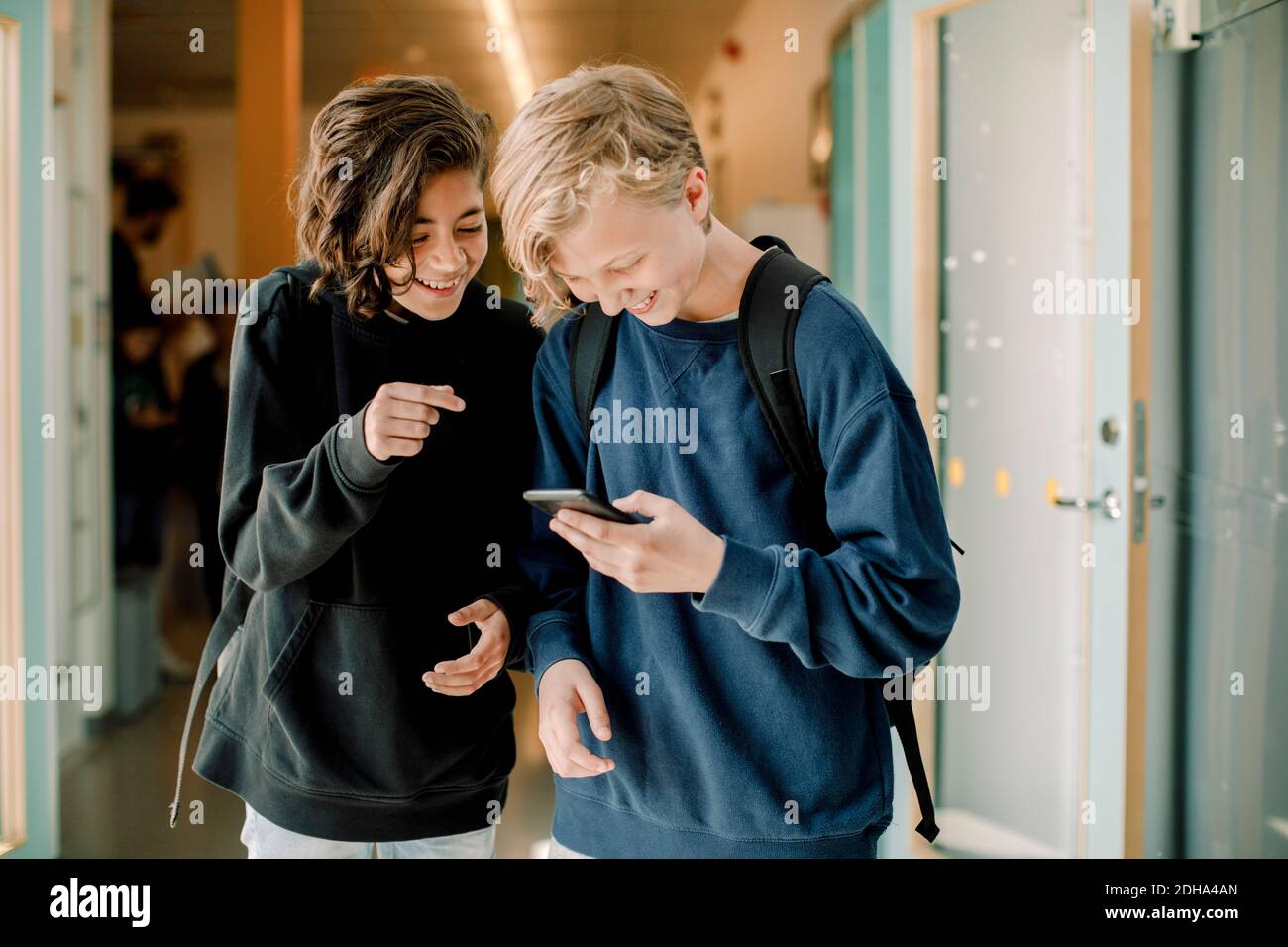 Smiling male students using smart phone in school corridor Stock Photo ...