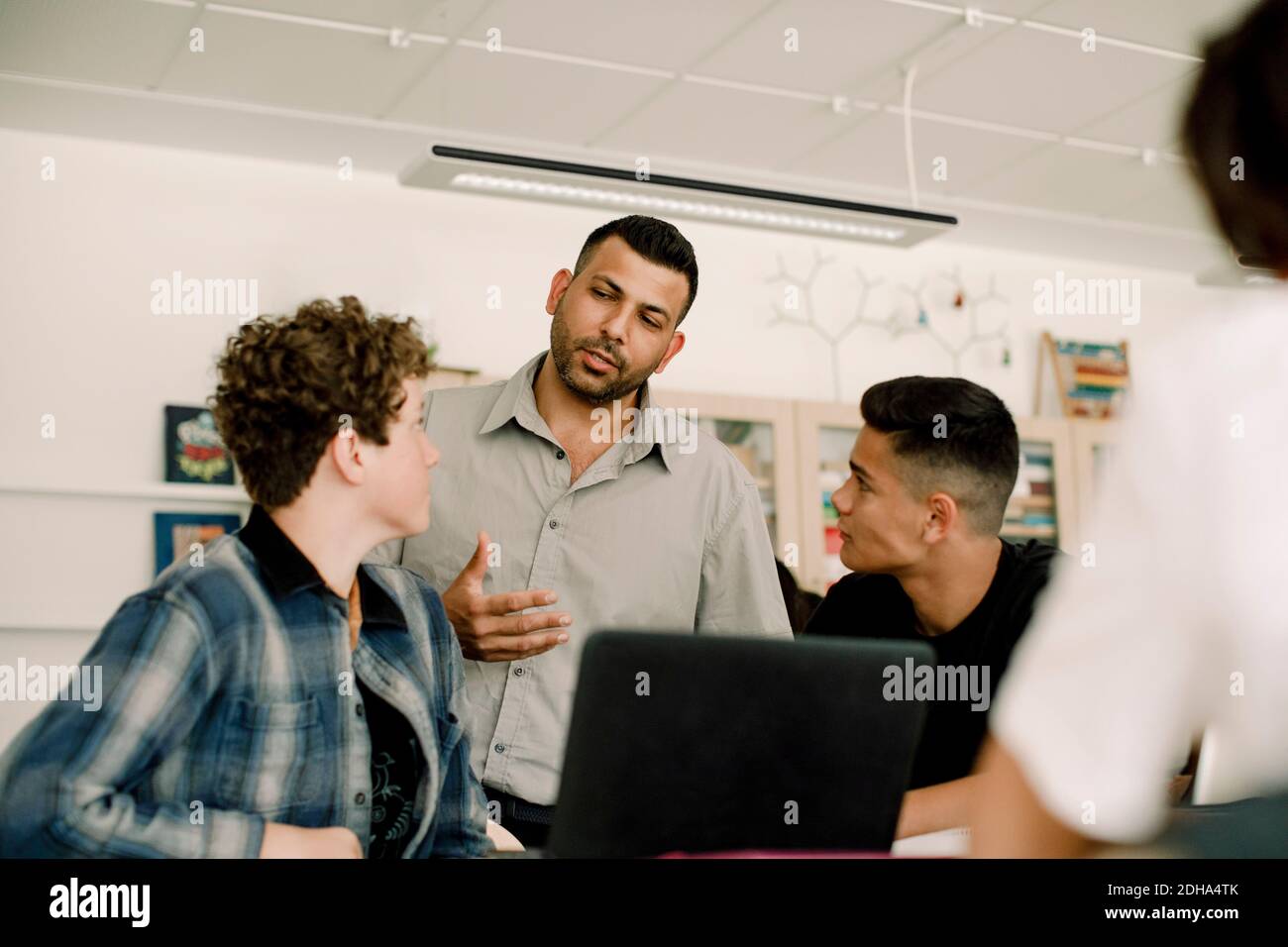 Professor discussing with male students while standing in classroom ...