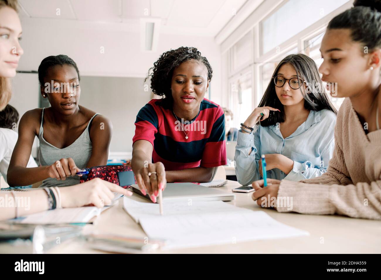 Teacher explaining while female students studying by table in classroom ...