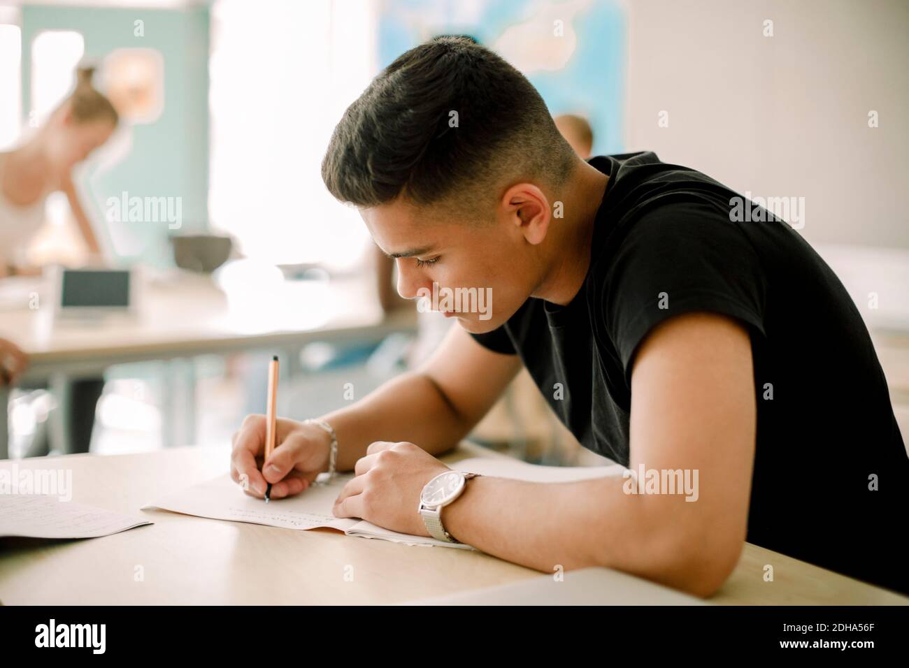 Teenage boy studying while sitting by table in classroom Stock Photo ...