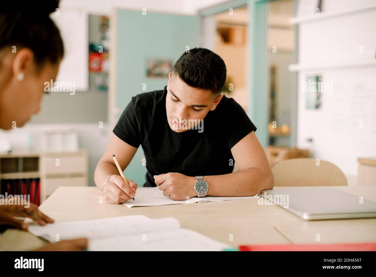Male teenager writing while sitting in classroom Stock Photo - Alamy