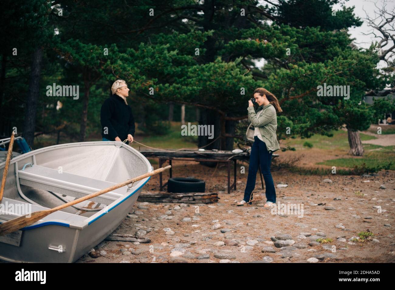 Young woman photographing friend standing by boat at beach Stock Photo ...