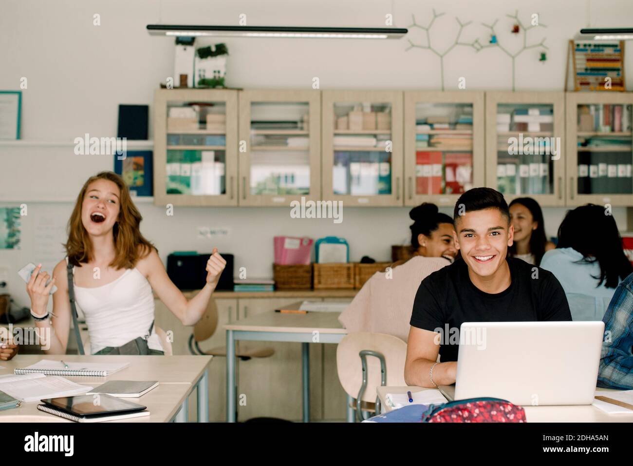 Portrait of male students using laptop while smiling female teenagers ...