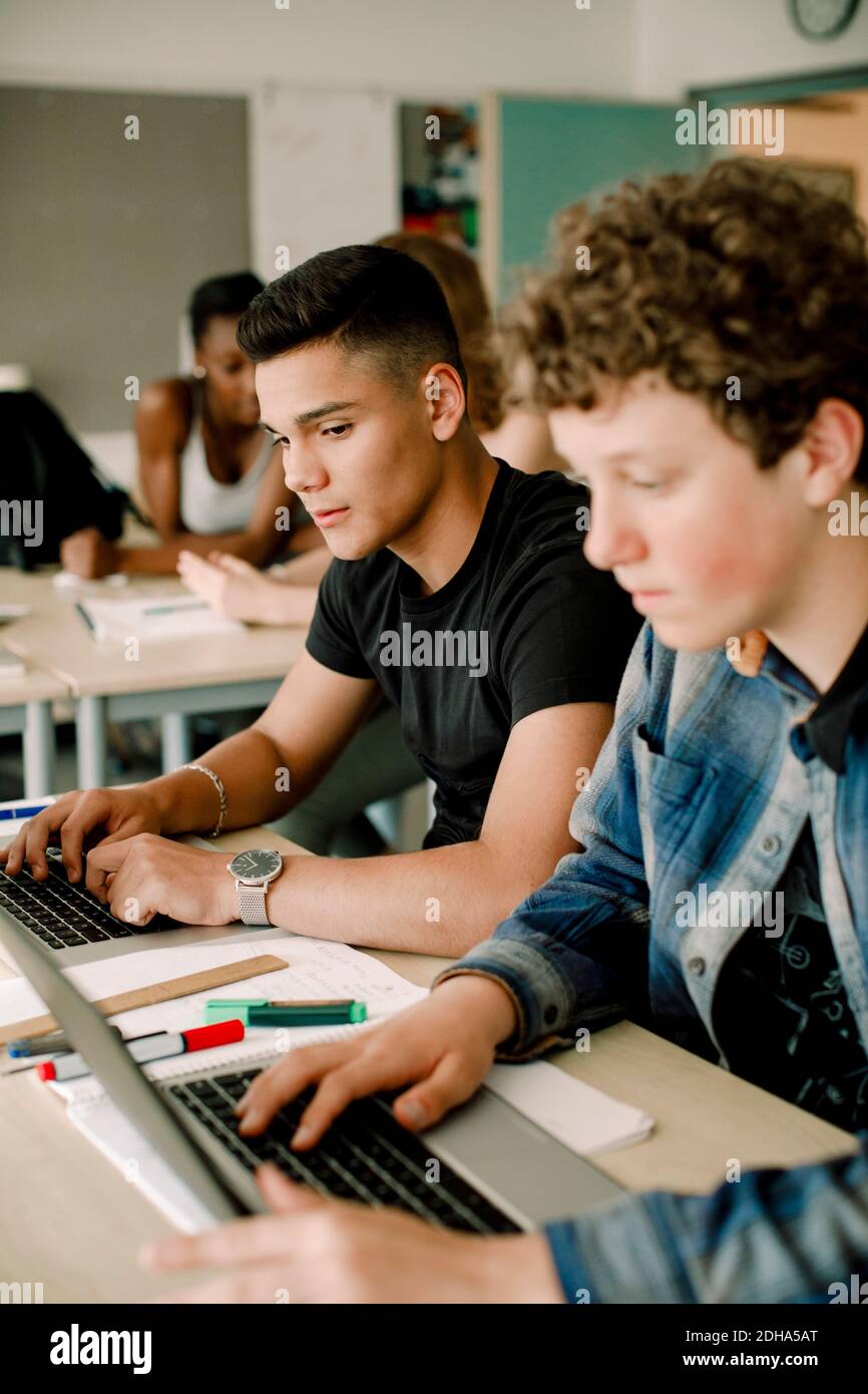 Male students using laptop while sitting by table in classroom Stock ...
