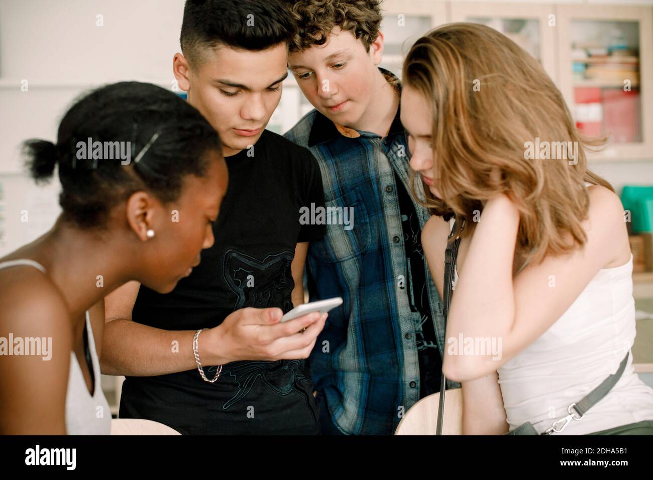 Male student using phone while standing by friends in classroom Stock ...
