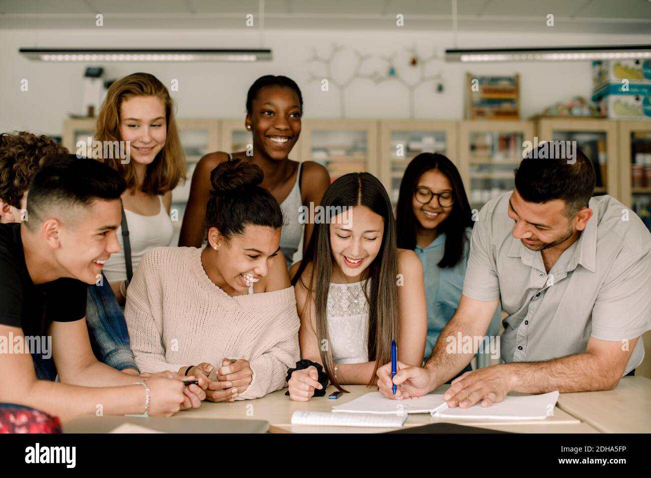 Smiling tutor teaching male and female students while leaning over ...