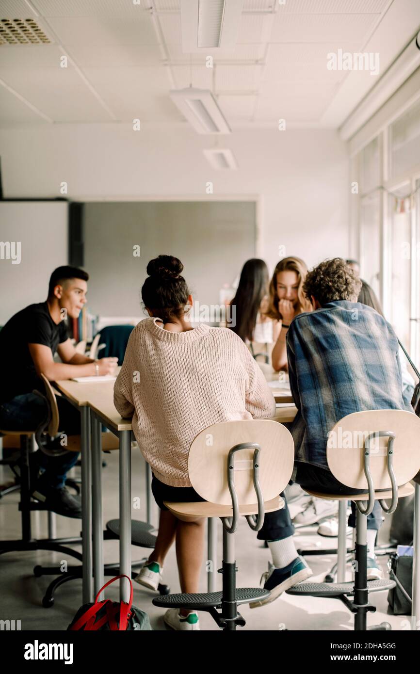 Rear view of teenage students studying by table in classroom Stock Photo - Alamy