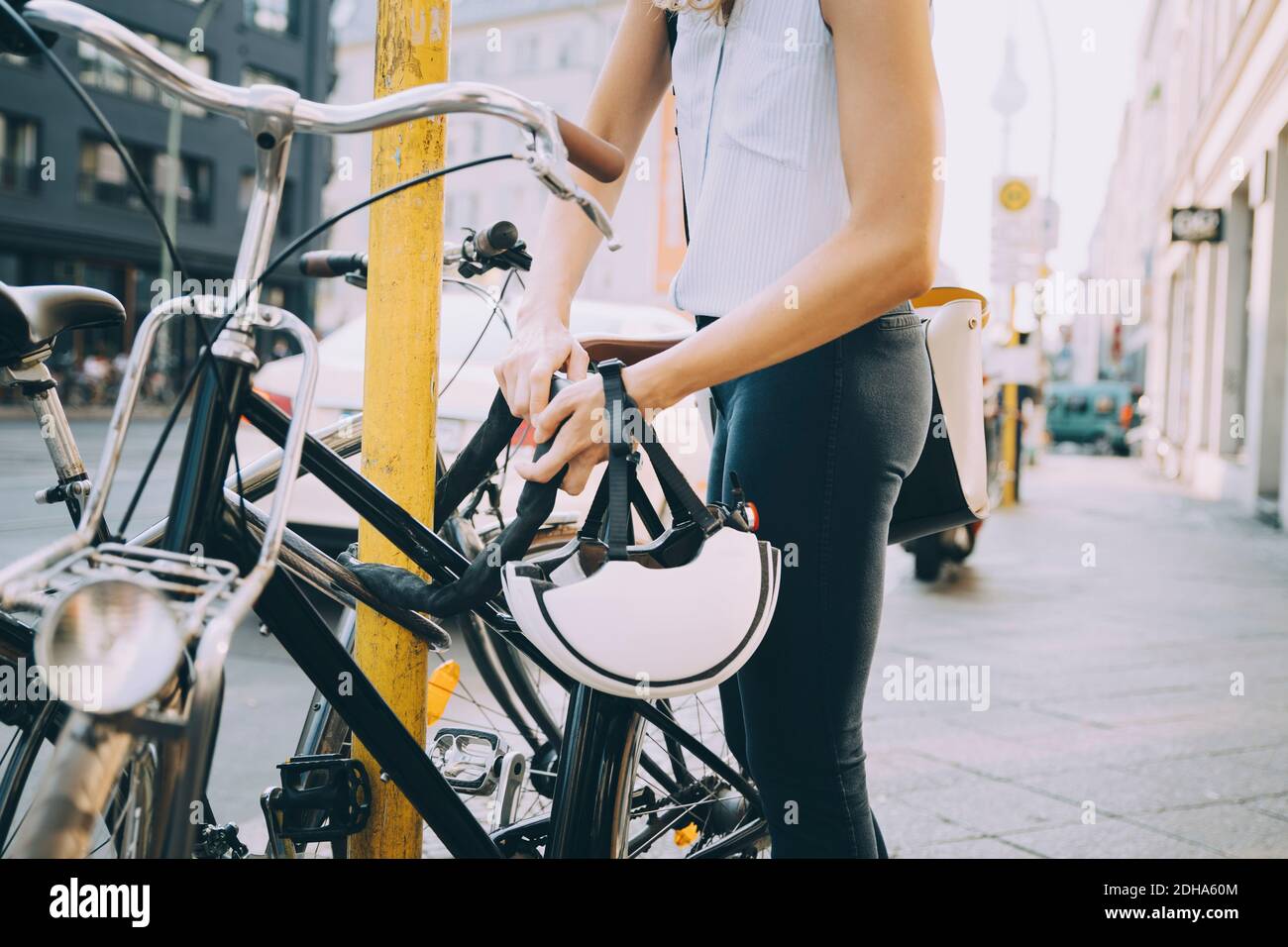 Midsection of businesswoman locking bicycle with pole on sidewalk in ...